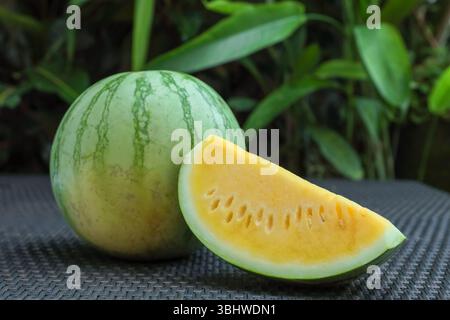 Whole and cut yellow watermelons on wicker table near swimming pool ...