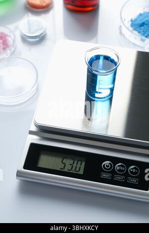 Scale with beaker of sample and other laboratory equipment on white ...