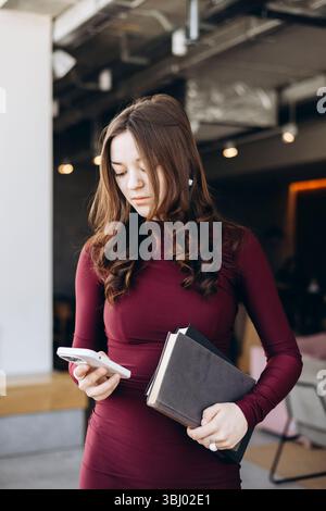 A female student in a maroon dress stands thoughtfully in an academic ...