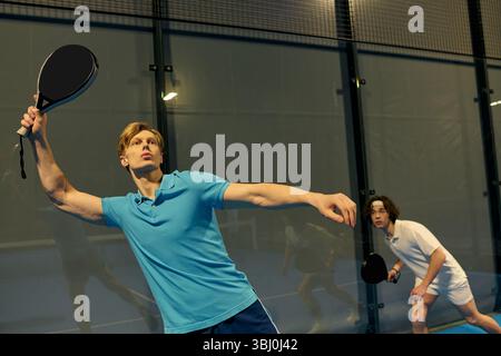 Two young sportsmen engage in an intense padel match, demonstrating ...