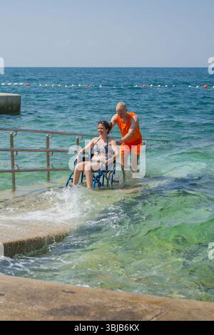 Relaxed woman with disability, exiting the sea water with the help of ...