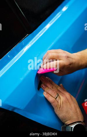 Detailing expert uses red squeegee wrapper to flatten blue PPF wrap on ...