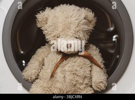 Plush bear sitting on washing machine Stock Photo - Alamy
