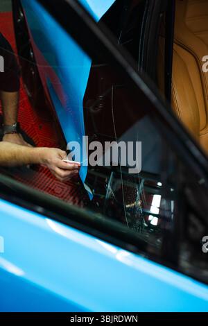 Detailing expert uses red squeegee wrapper to flatten blue PPF wrap on ...