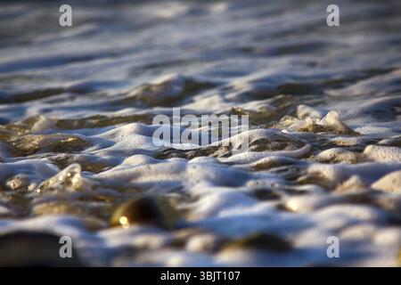 Beach of multi-colored round pebbles, foam and splash of salty waves ...