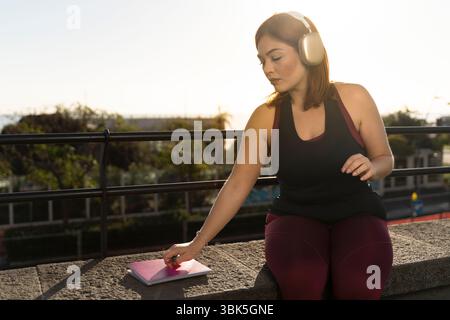 freelancer in headphones writing in notebook near laptop and smartphone ...