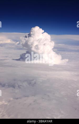 A dramatic vertical cloud formation rises above the lush green ...