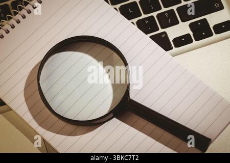 Magnifying glass on laptop keyboard, searching or data security concept ...