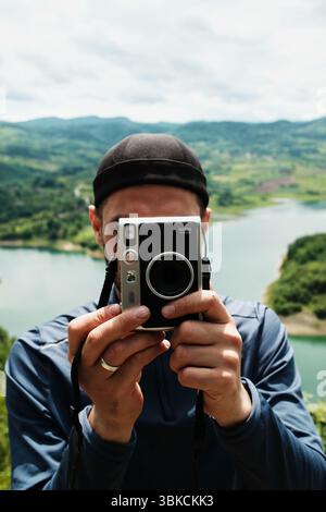 Man holding an Instax photo and camera, smiling while waiting for image to develop outdoors ...