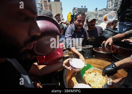 Palestinians wait in long queues to receive pots of food distributed by ...