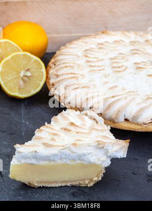 Portion of lemon tart with meringue and lemons decoration on a black ...