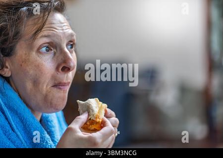 A woman is eating a sandwich and smiling. She is wearing a blue robe ...