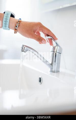 Woman's hand turning faucet Stock Photo - Alamy