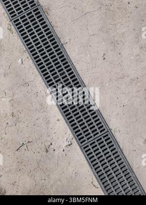 Rectangular metal drain grate set into a dry earth. There is a slight ...