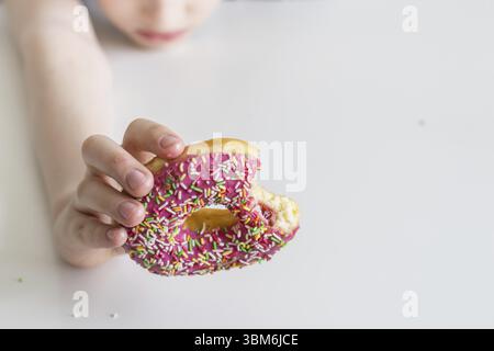 Children's hand stretches a bitten donut in a pink glaze. Banner format ...