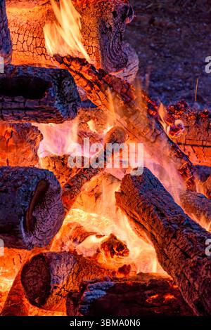 Wood logs burning during a dark night, producing orange flames and ...