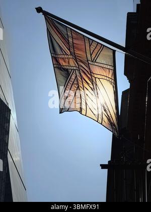 Union Jack flag backlit by the sun on a flagpole facing to the right ...