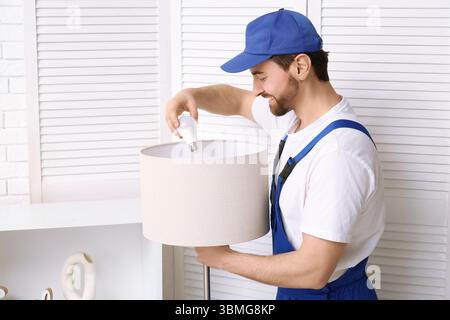 Happy male electrician changing light bulb in floor lamp at home Stock ...