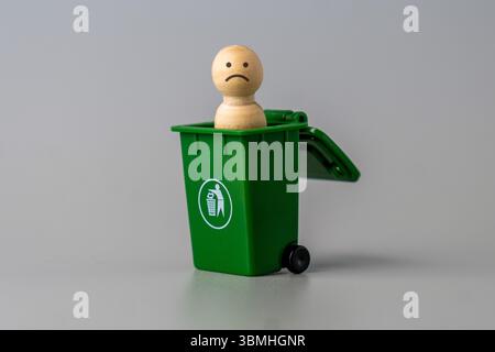 A small wooden figure with a sad face on it is placed inside a trash ...