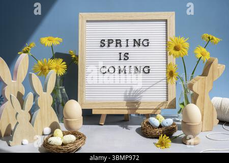 SPRING IS COMING text on letter board with bunny wooden figures and ...