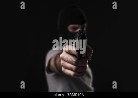 Masked robber with gun aiming into the camera against a black ...