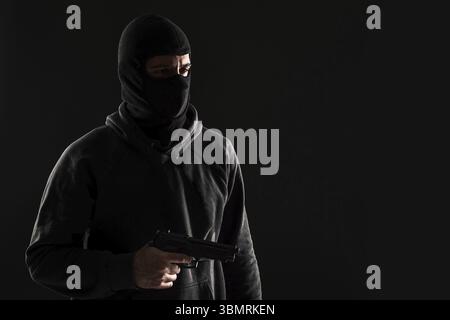 The robber in a mask with a gun pointed to the side on a black ...