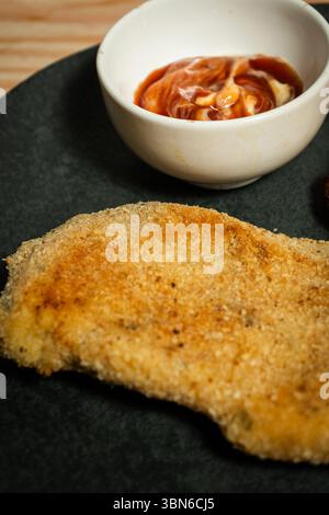 Golden brown breaded chicken cutlet on textured white plate. Rustic ...