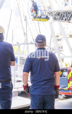 Firefighters in uniform stand by a fire truck with a ladder, looking ...