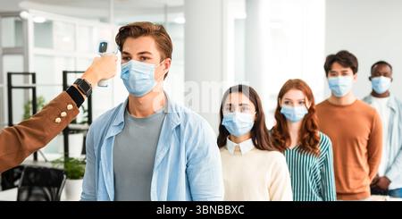 Teacher with contactless thermometer cheking temperature of multiracial ...