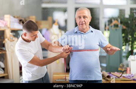 Young man tailor takes body measurements from elderly man Stock Photo ...