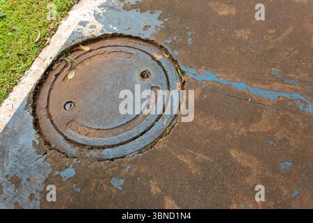 Round hole with a smiley face drawn on it. The hole is on a sidewalk ...