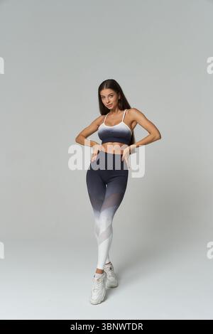 The athletic woman stands poised against gym bars, her focused gaze and ...