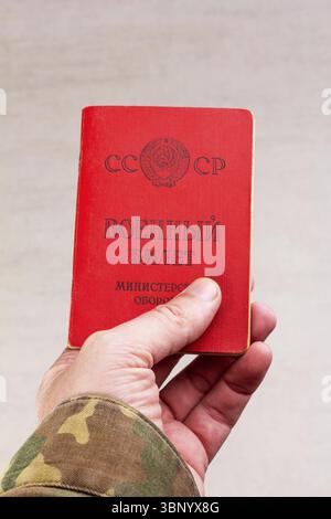 Russian military ID in male hands on wooden table. Translation of ...