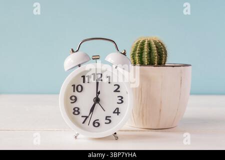 White alarm clock with cactus in pot on wooden desk. Minimal time ...