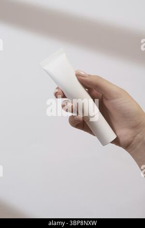 Woman's hand presents a mockup of a white plastic tube of hand cream ...