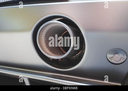 Car engine single exhaust metal tip close up shot next to rear bumper ...