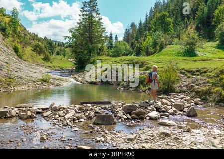 Hiker crossing rocky rural stream Stock Photo - Alamy