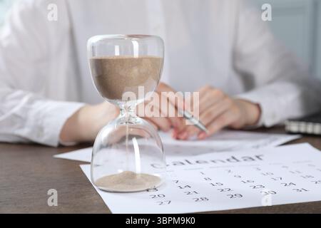 Deadline. Woman with calendar and pen at wooden table in office, focus ...