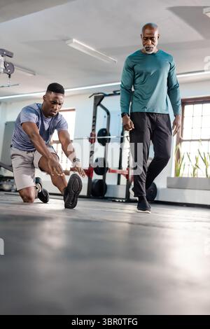African American trainer guiding client performing overhead dumbbell ...