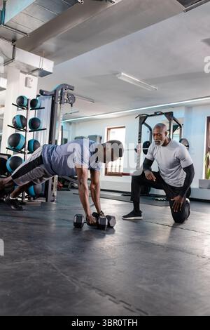 African American trainer and client performing squat workout at fitness ...