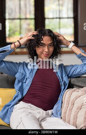 Non-binary person adjusting curly hair in bathroom near window with ...