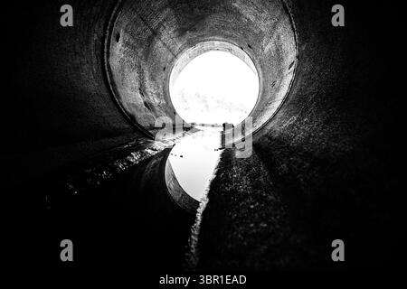 Inside a circular concrete drainage culvert with a trickle of water ...