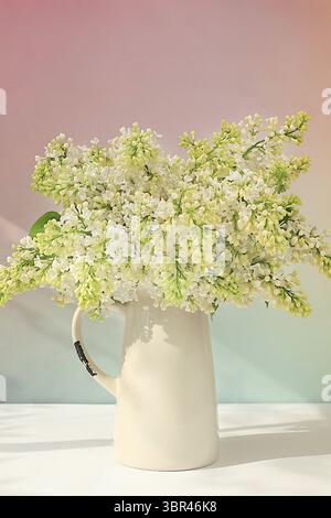 Vase with bouquet of beautiful white lilac and teapot on table against ...