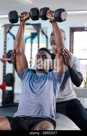 Senior African American trainer guiding client performing weighted ...