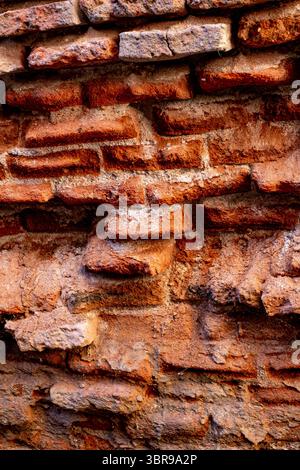 A close-up of a beat-up red brick wall with rough, uneven bricks in ...