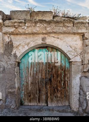Door with a door knocker in an old stone wall overgrown with plants ...