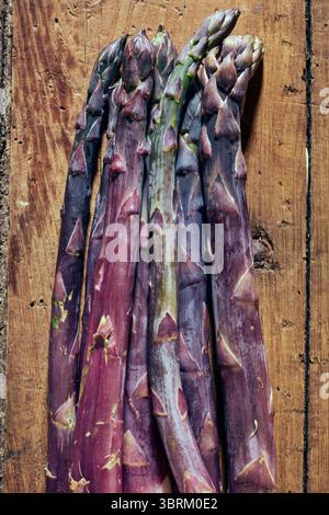Bunch of fresh green and purple asparagus spears on dark textured wood ...