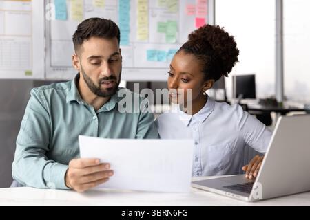 Two colleagues brainstorming finance strategy at laptop during office ...