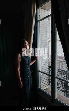 Woman looking out of tall shuttered window in Paris apartment Stock ...