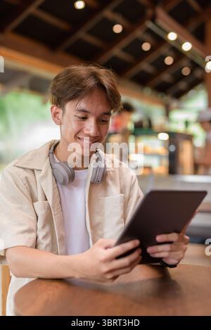 Handsome young Asian non binary man sitting in cafe restaurant using ...